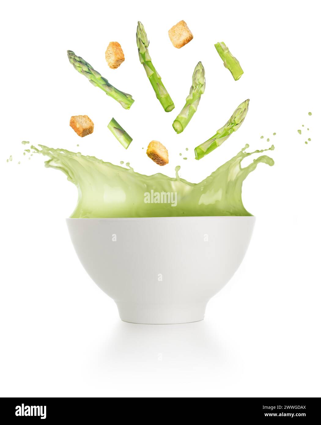 Asparagus and croutons falling into a creamy soup bowl splashing on ...