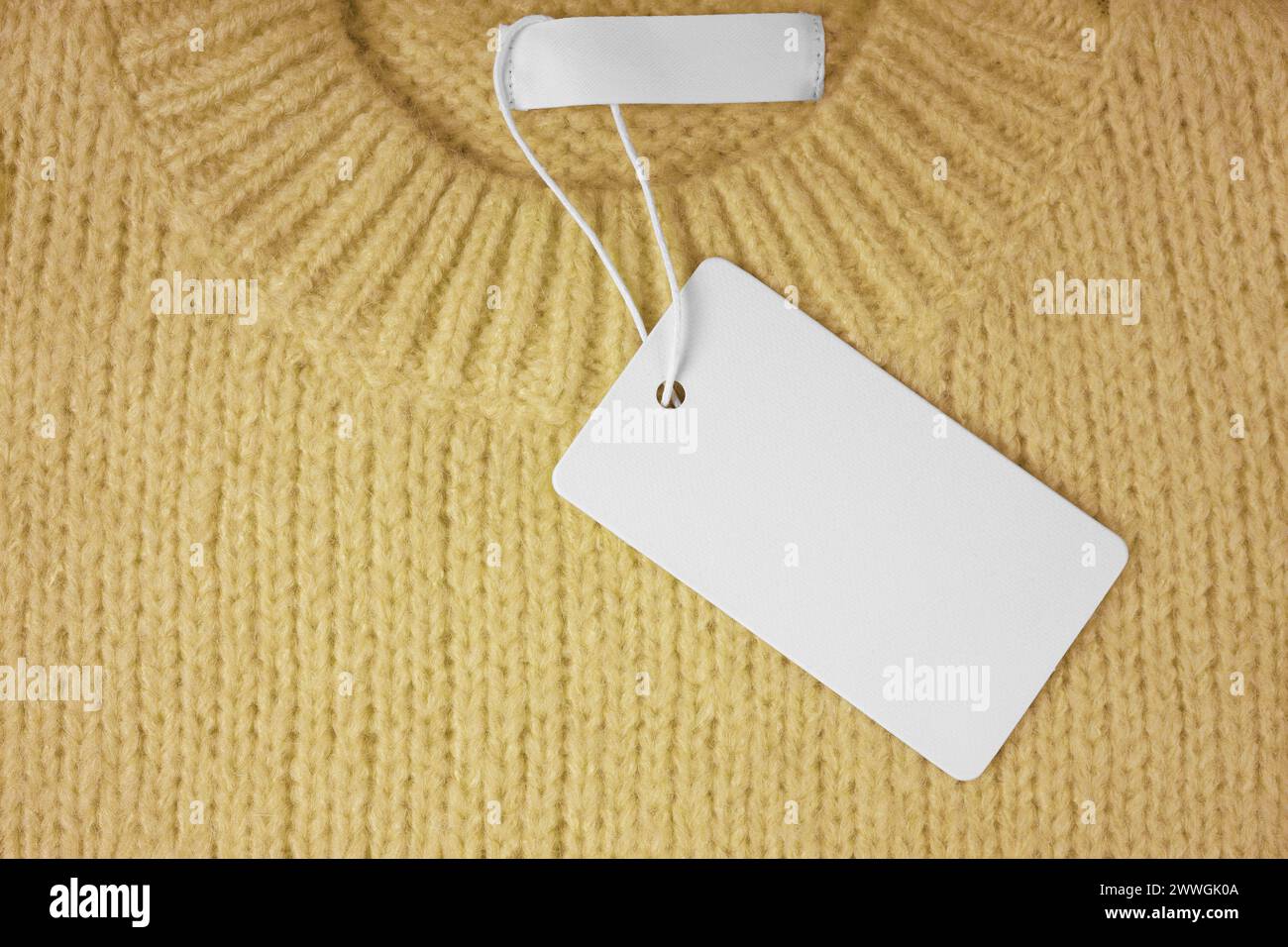 Blank clothing tag and inner label on neck of yellow knitted sweater ...