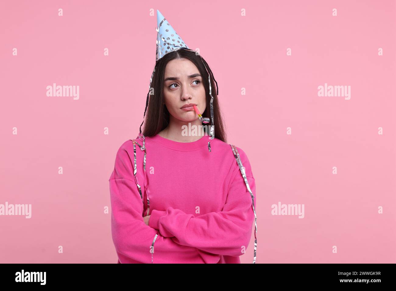 Sad woman in party hat with blower and streamers on pink background ...
