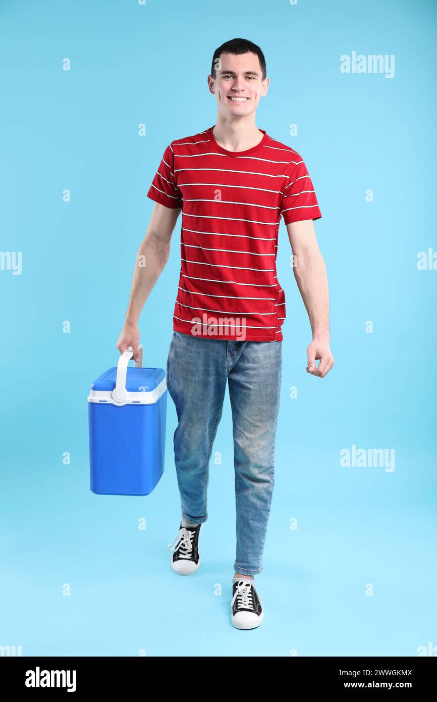 Man with cool box walking on light blue background Stock Photo - Alamy
