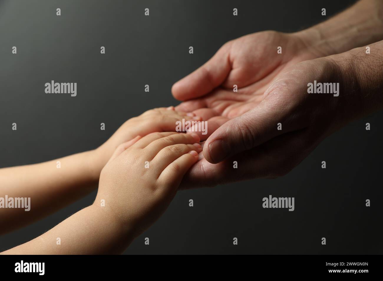 Father and child holding hands on dark grey background, closeup Stock ...