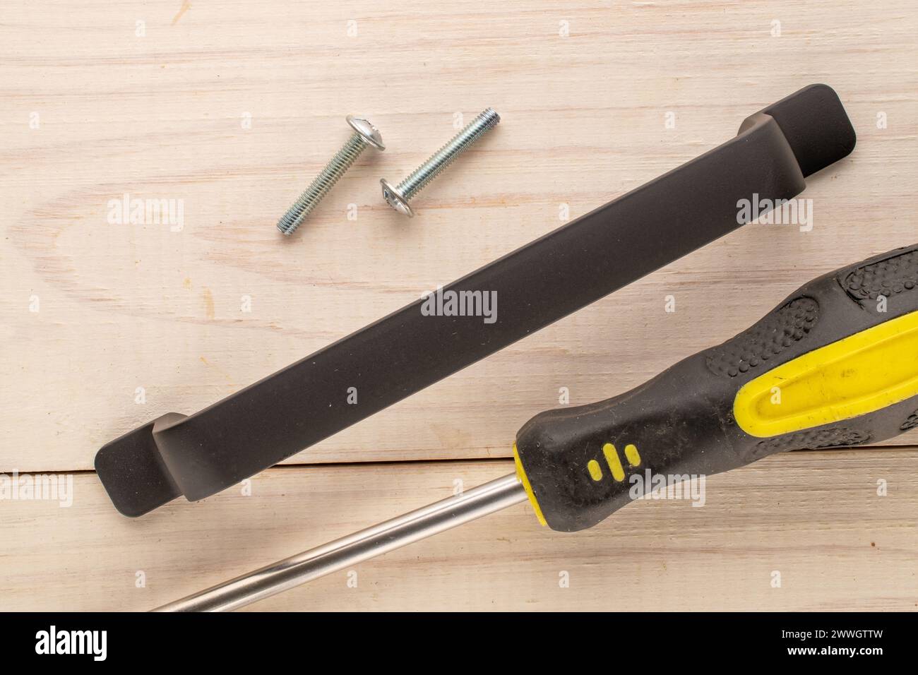 One metal drawer handle, screwdriver and two screws on wooden table ...