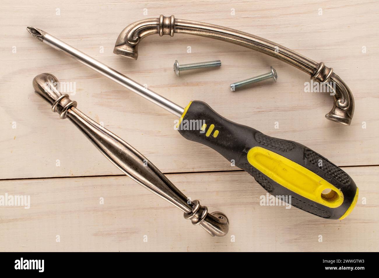 Two metal drawer handles, a screwdriver and two screws on a wooden ...