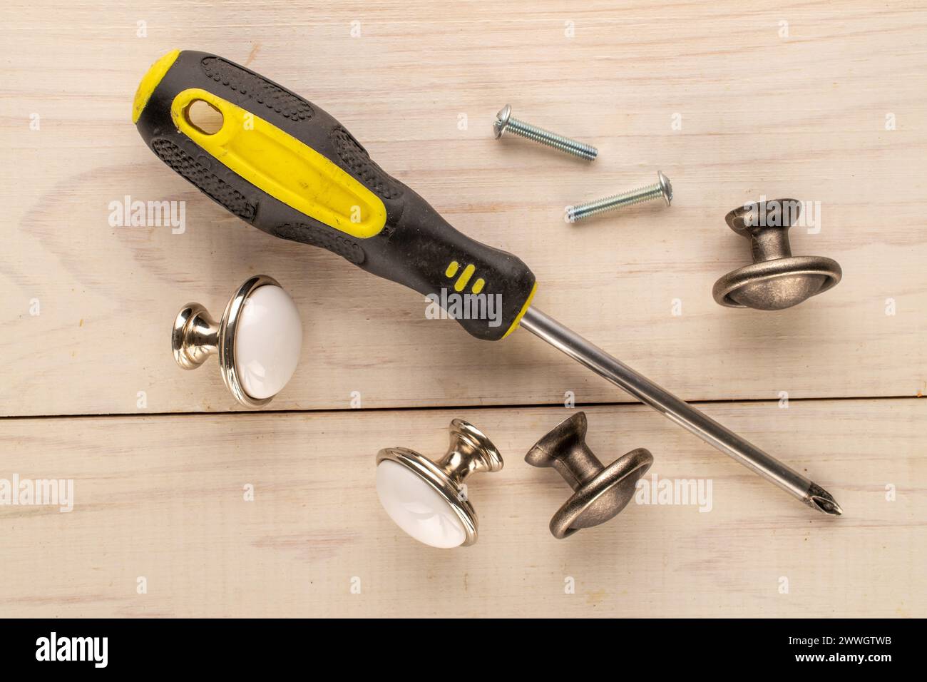 Four metal drawer handles, screwdriver and two screws on wooden table ...