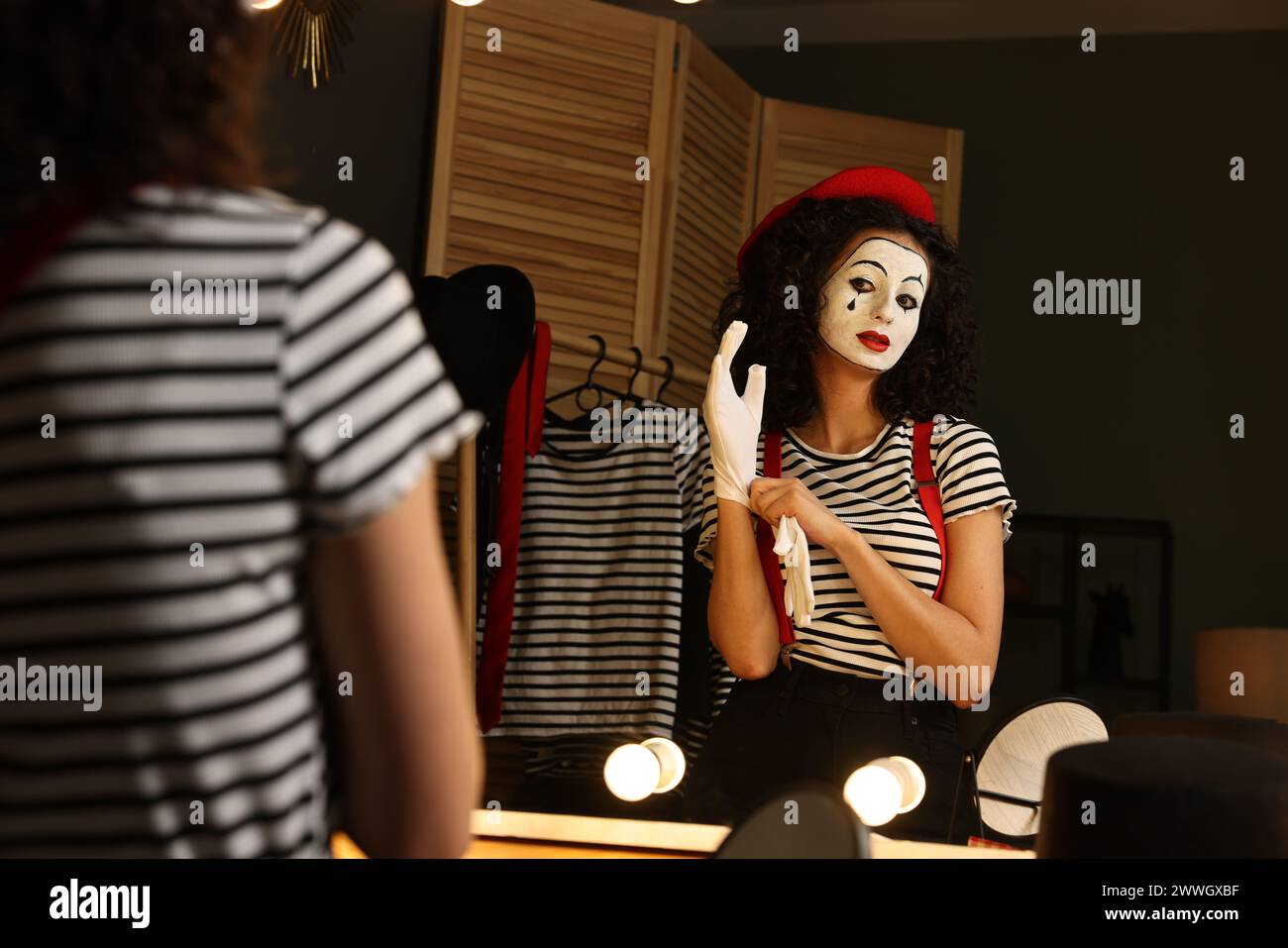 Young woman in mime costume putting gloves near mirror indoors Stock ...