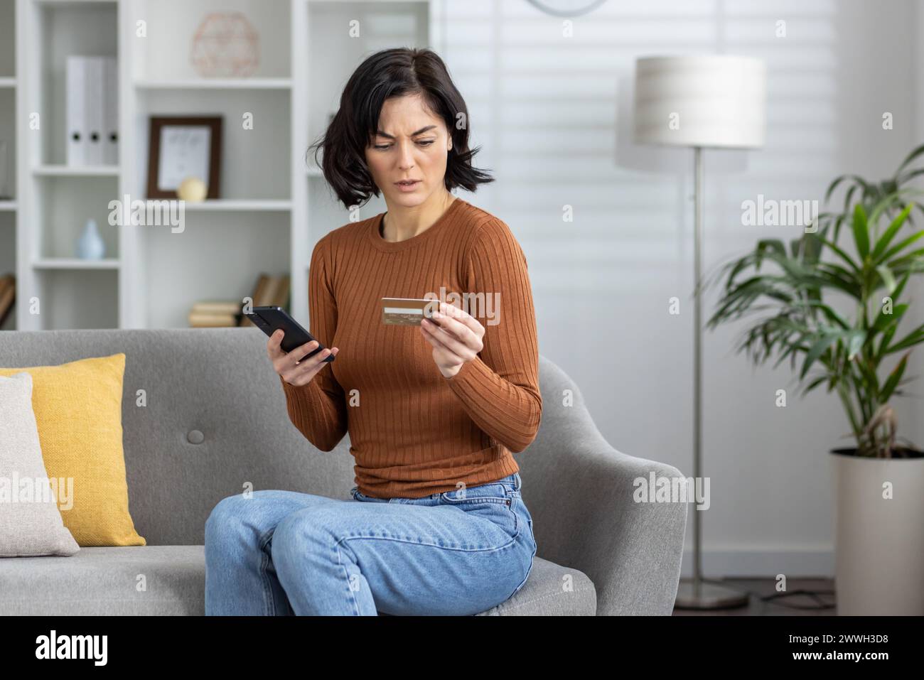 An alarmed woman indoors using a smartphone and credit card, facing a ...