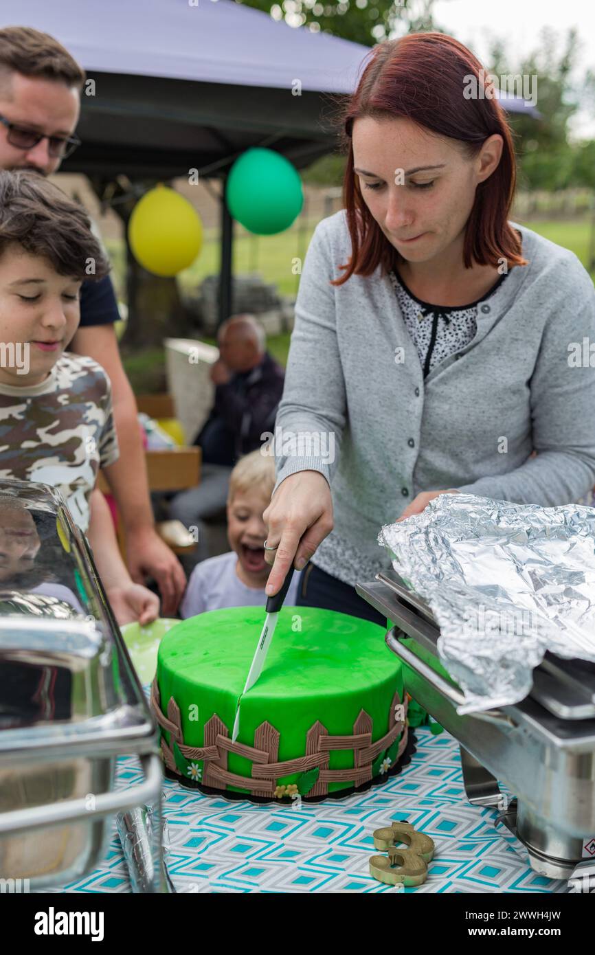 A family celebrating a birthday. The mother is cutting the cake with a ...