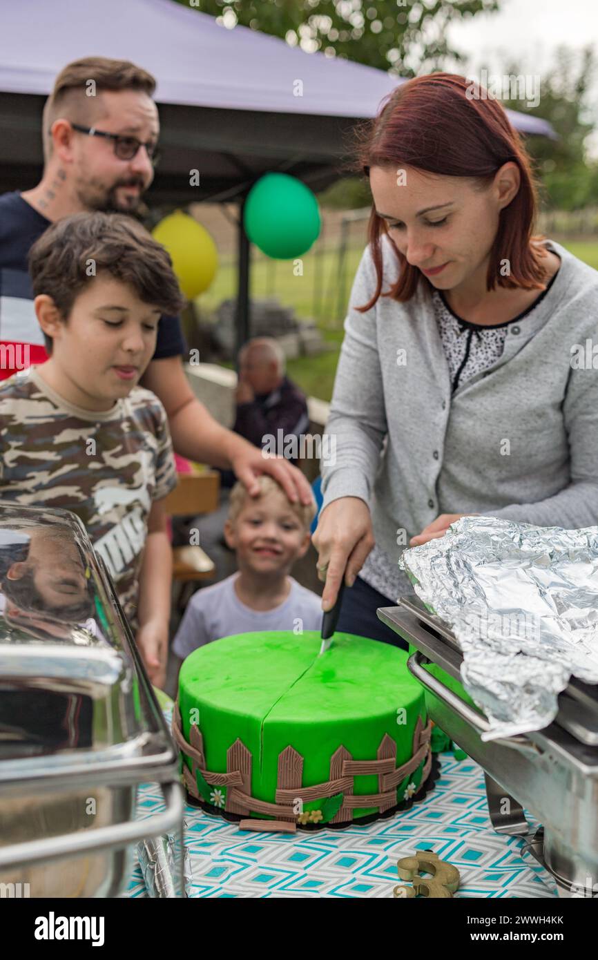 A family celebrating a birthday. The mother is cutting the cake with a ...