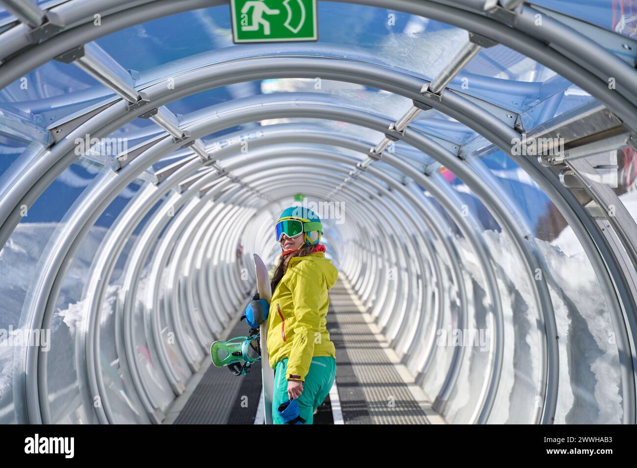 Rear view of a snowboarder with colorful gear in a transparent tunnel ...