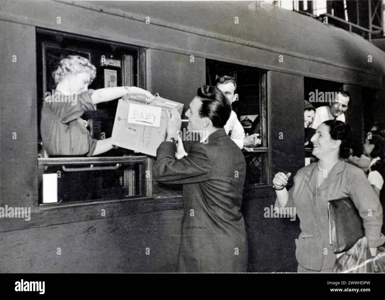 young man smoking cigarette hands cardboard box labeled „baby“ through ...