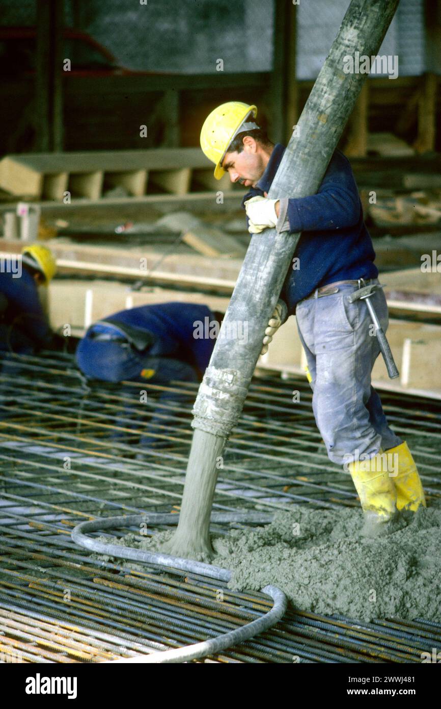 Workers piping concrete into foundations during construction of road ...