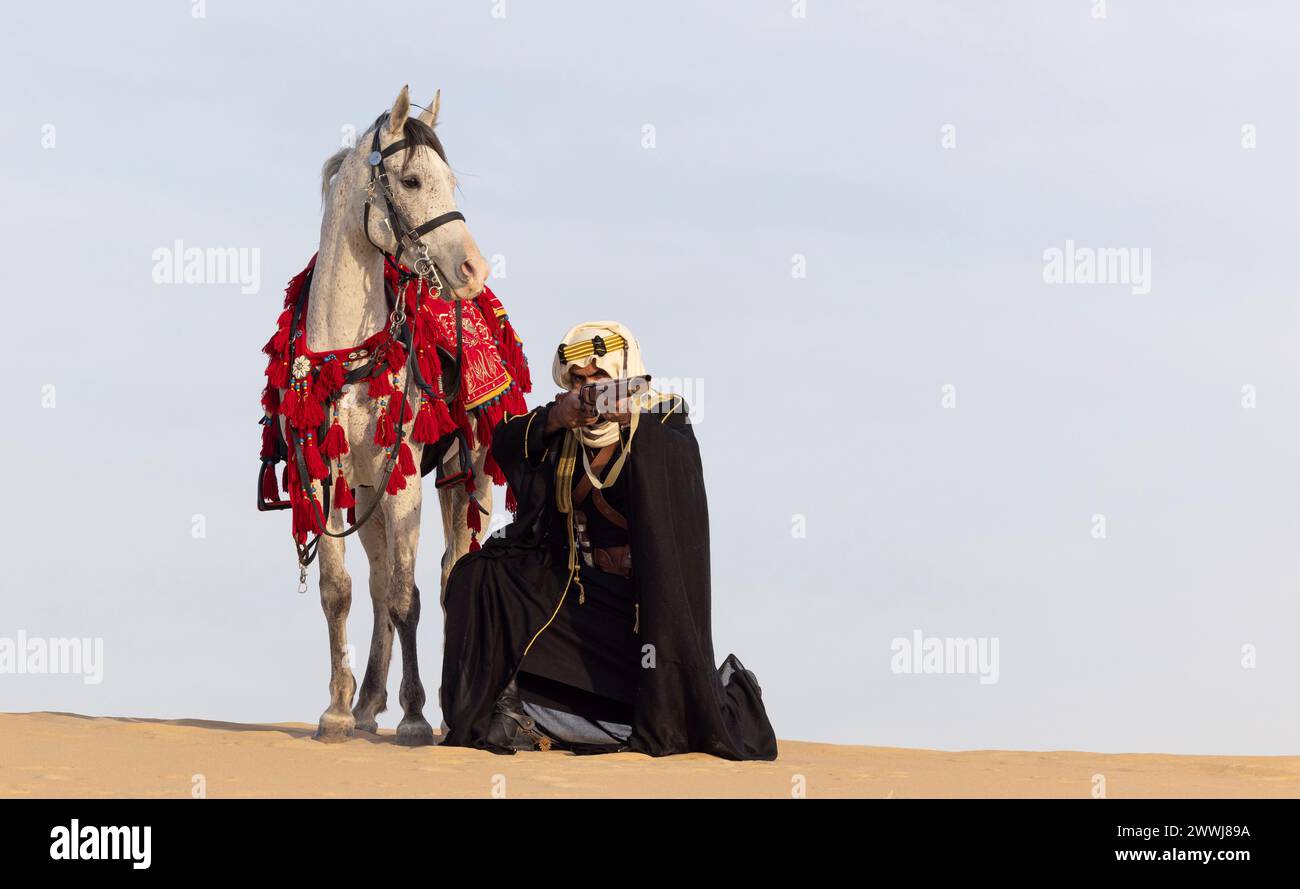 Saudi man in traditional clothing with his white stallion in a desert ...