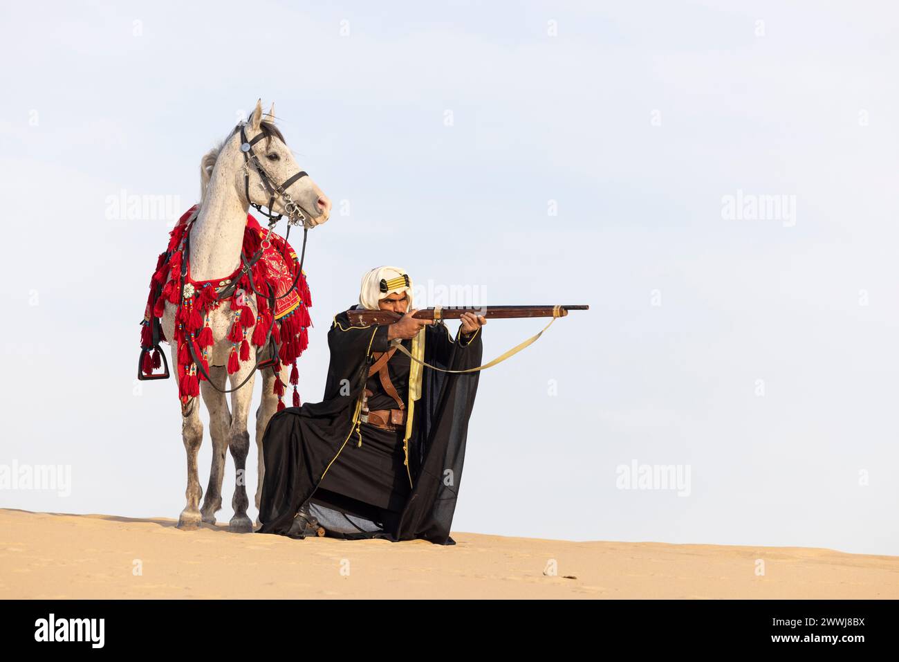 Saudi man in traditional clothing with his white stallion in a desert ...
