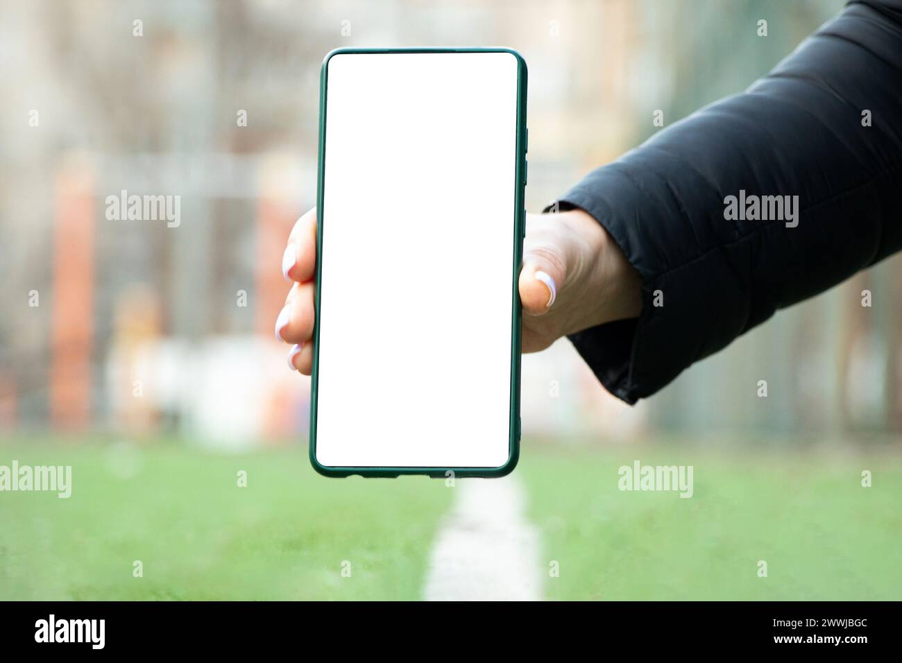 A woman's hand holds a phone with a white screen on a football field ...