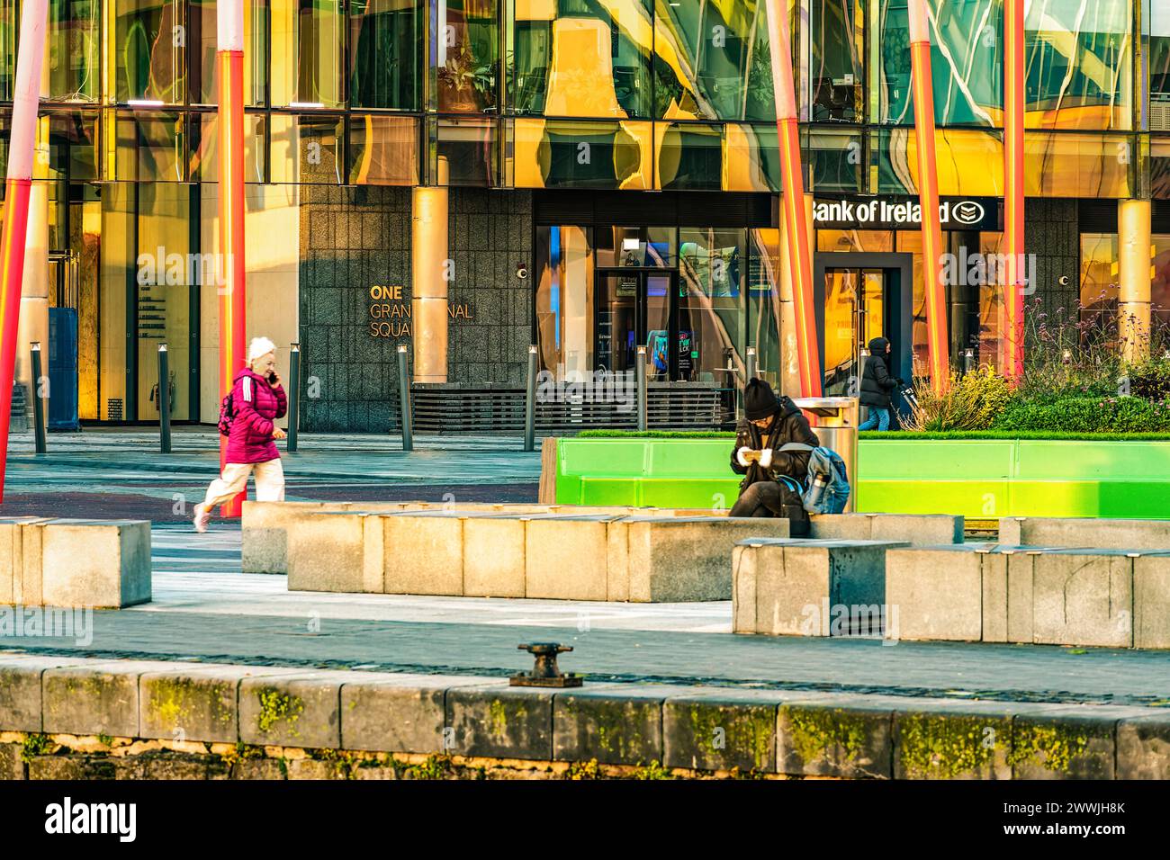 A young woman is sitting on a concrete bench and looking into her phone ...
