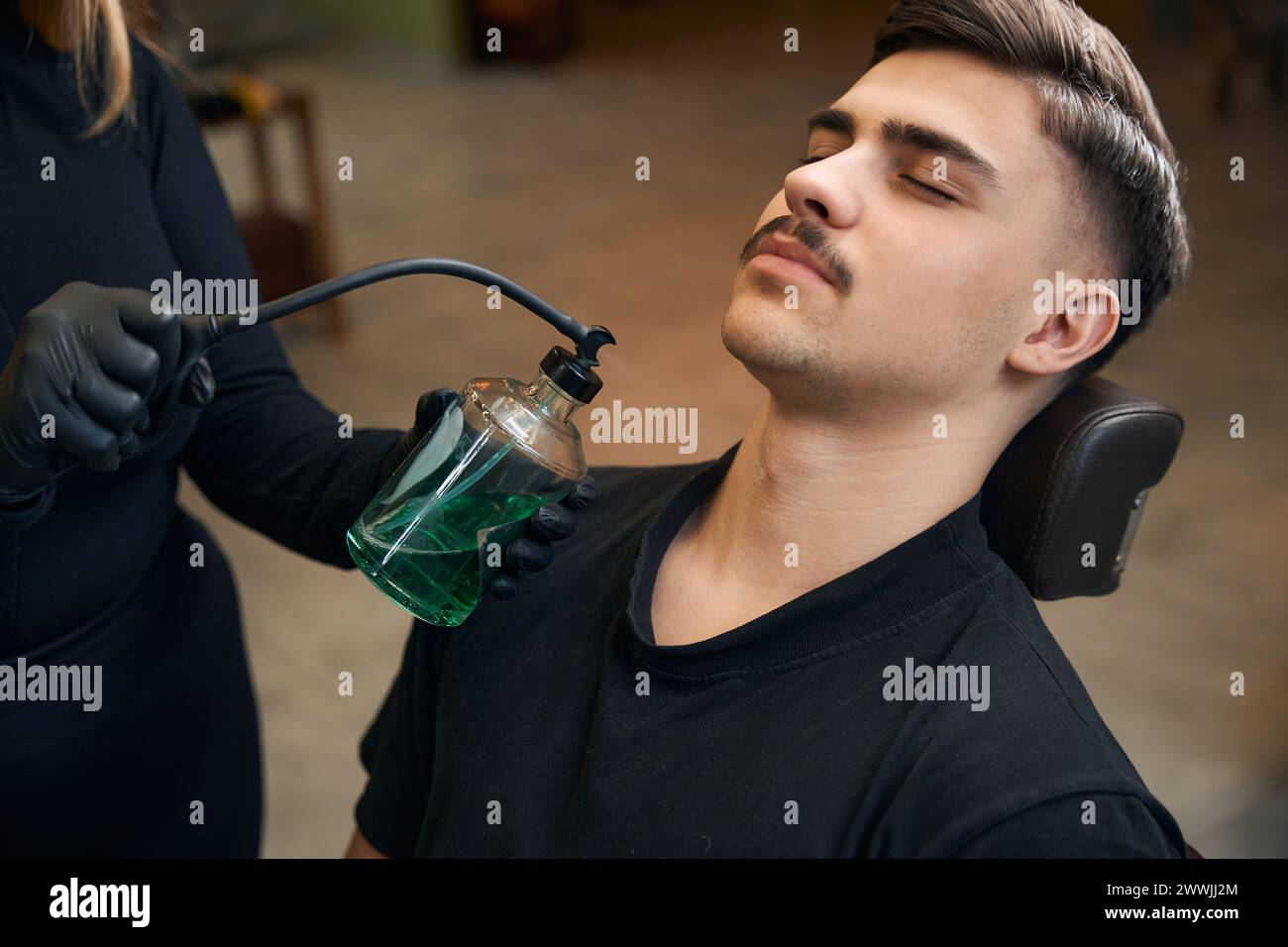 Woman barber spraying perfume on customer's hair in barbershop Stock ...