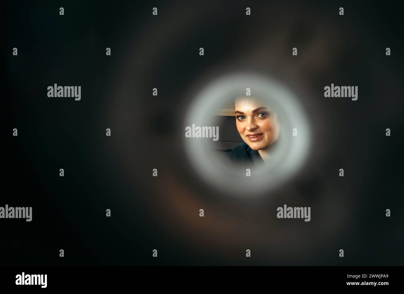 A woman peeks through a hole in a concrete wall, with curiosity and ...