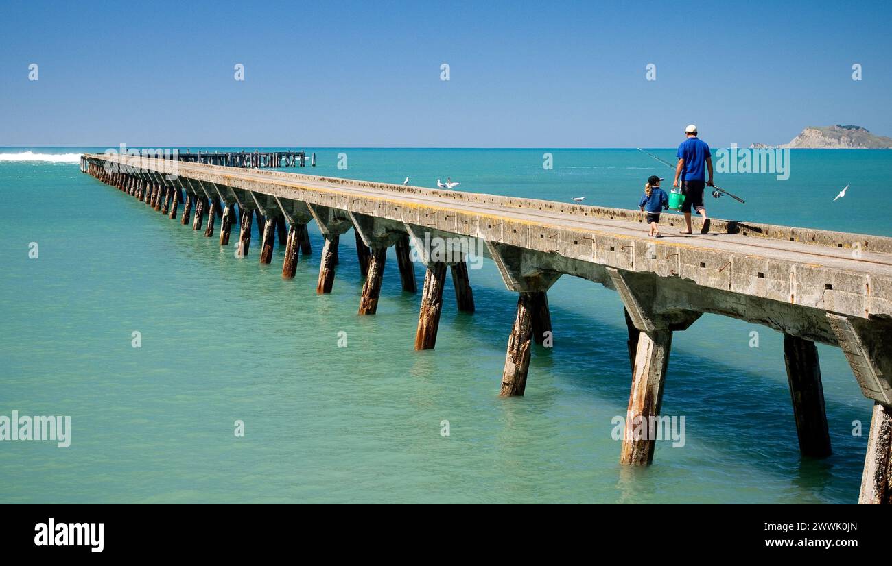 Father and son walking along the wharf to go fishing at Tokomaru Bay on ...