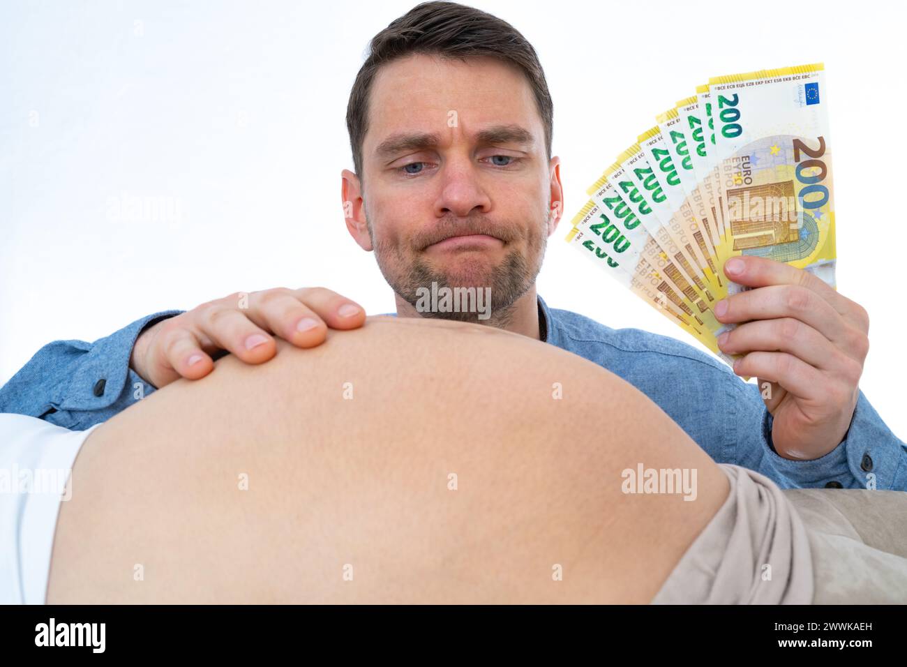 Description: Expectant father with banknotes in hand thoughtfully holds ...