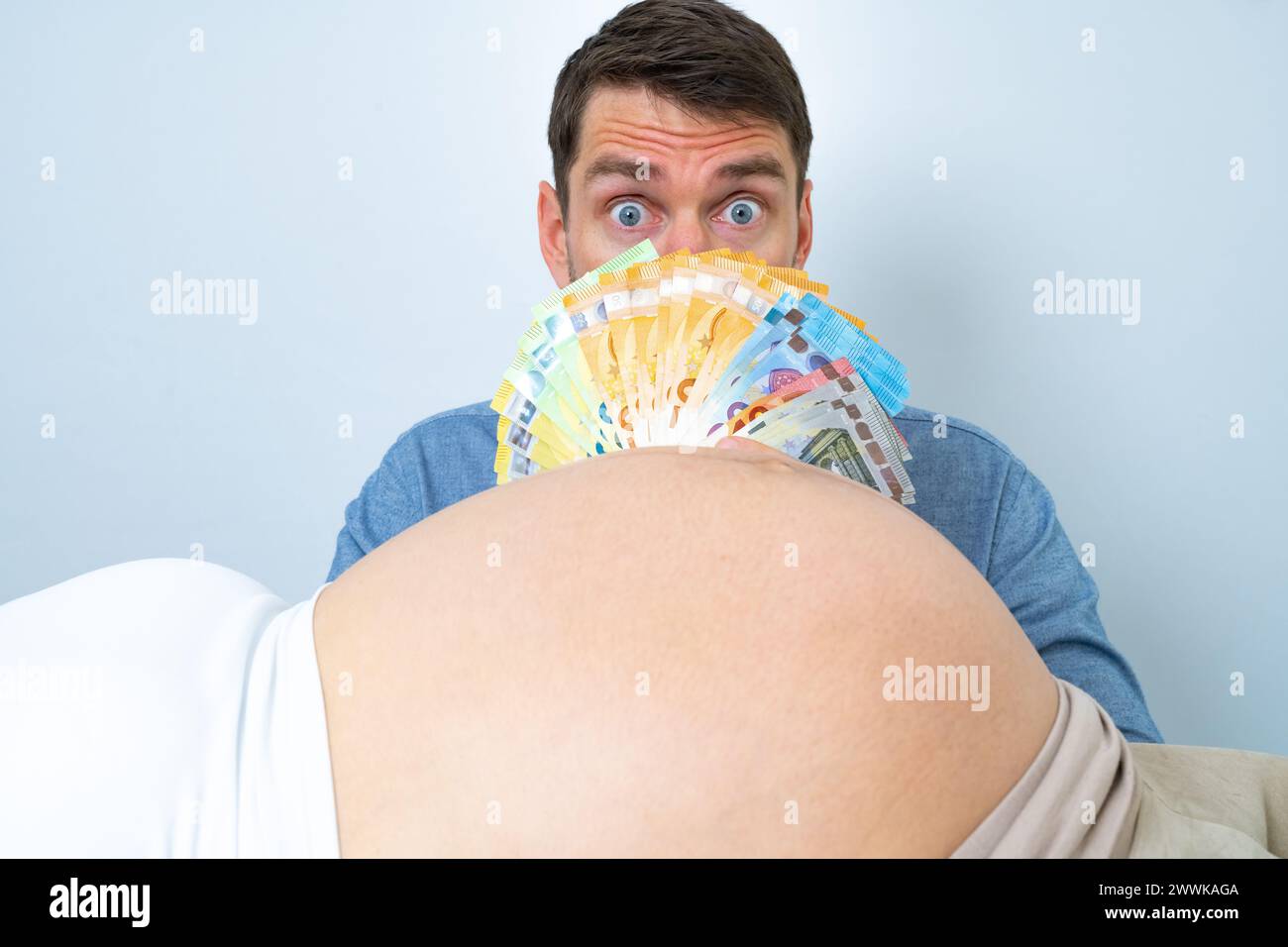 Description: Expectant father behind of pregnant baby bump holds a ...