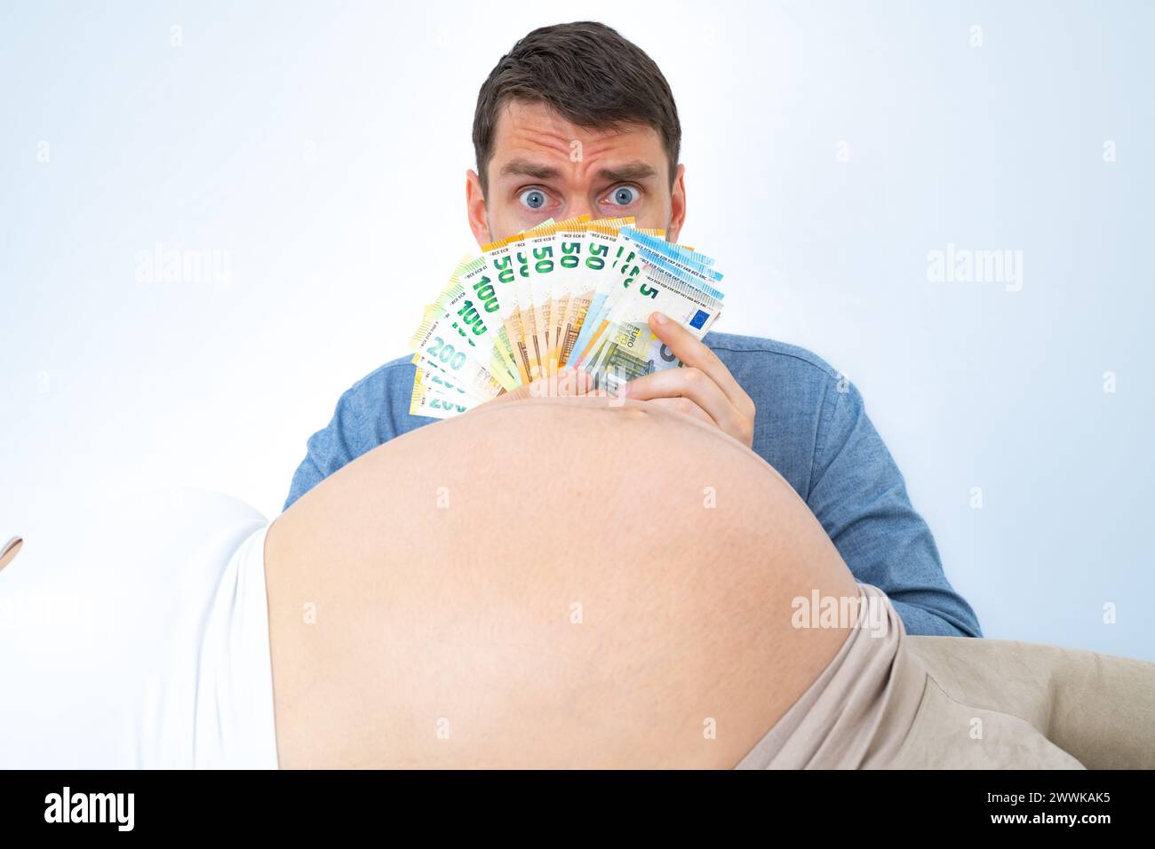 Description: Expectant father behind pregnant baby bump holds a stack ...