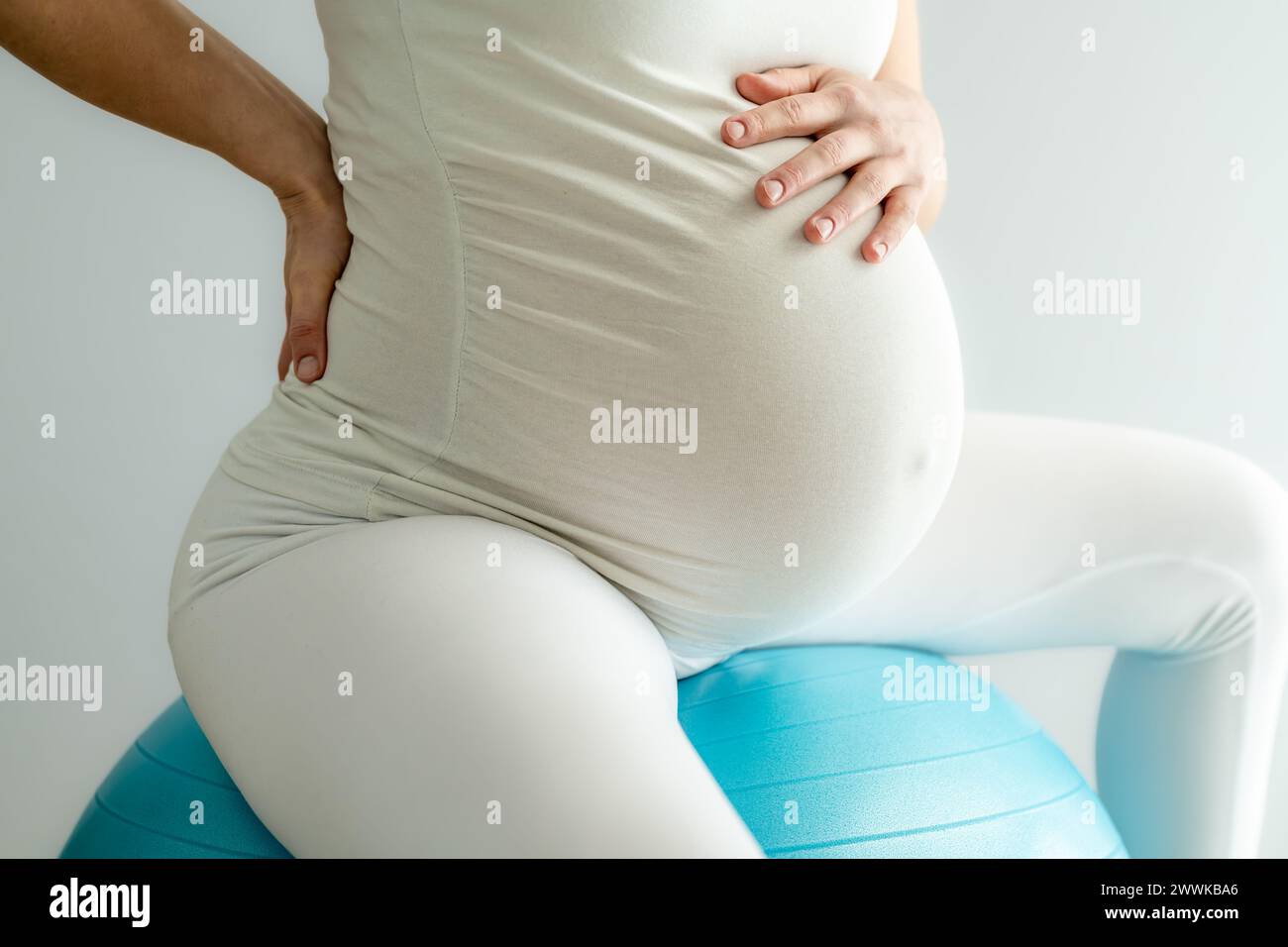 Description: Mother with heavily pregnant baby bump sitting on gym ball ...