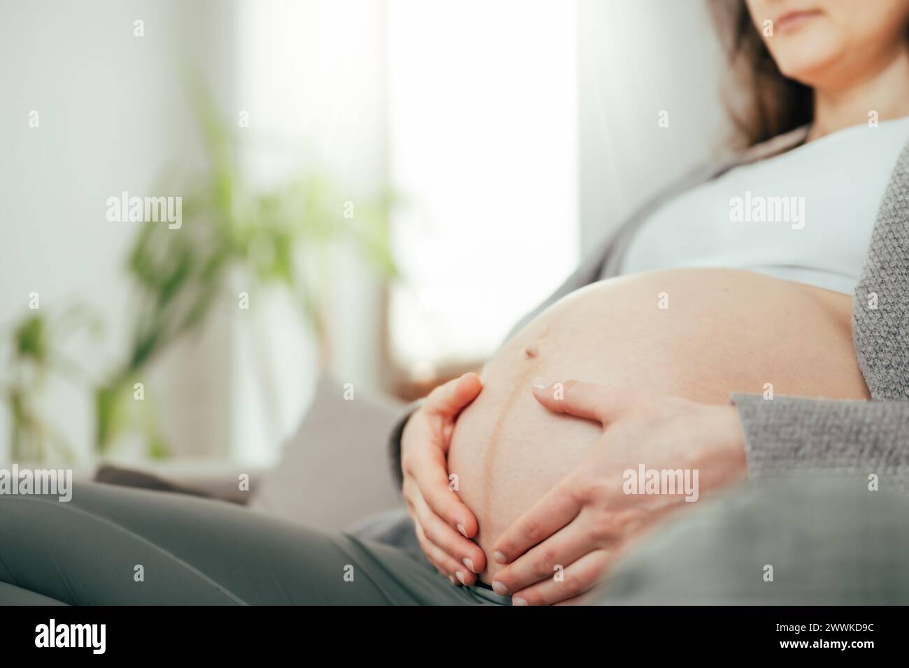 Description: Low angle view of woman sitting on sofa gently holding her ...