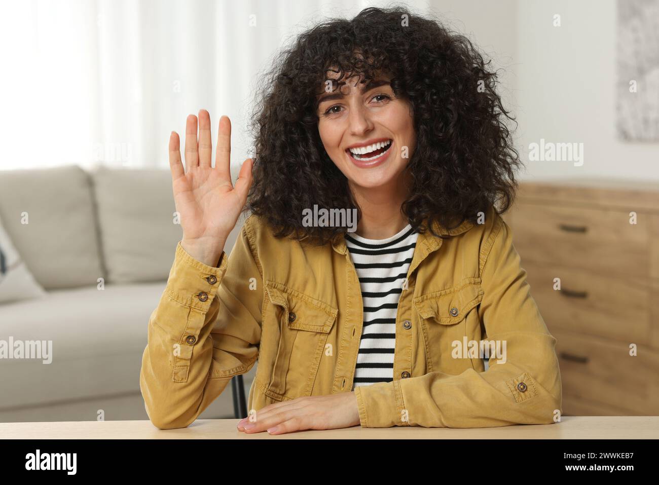 Happy woman waving hello at wooden table in room Stock Photo - Alamy