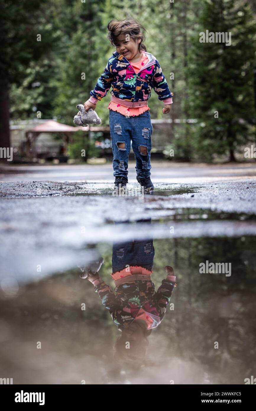 A young girl is standing in a puddle of water, holding a stuffed animal ...