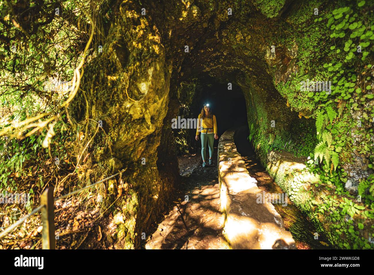 Description: Tourist woman exiting a tunnel along an overgrown jungle ...