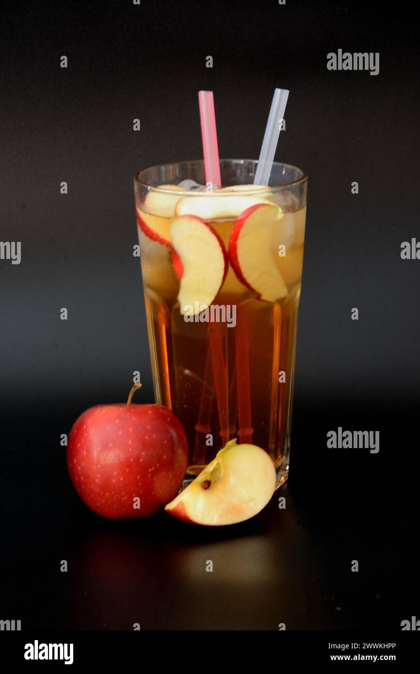 Refreshing fruit juice with ice and straws in a tall glass on a black ...