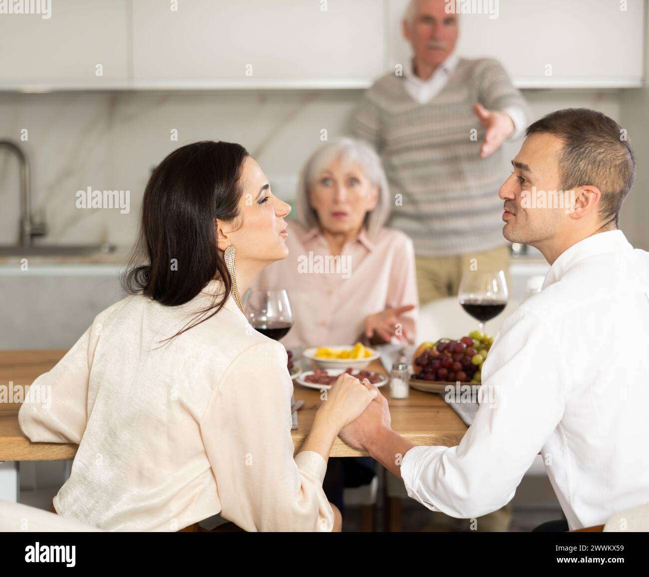 Romantic couple about to kiss with puzzled parents watching Stock Photo ...