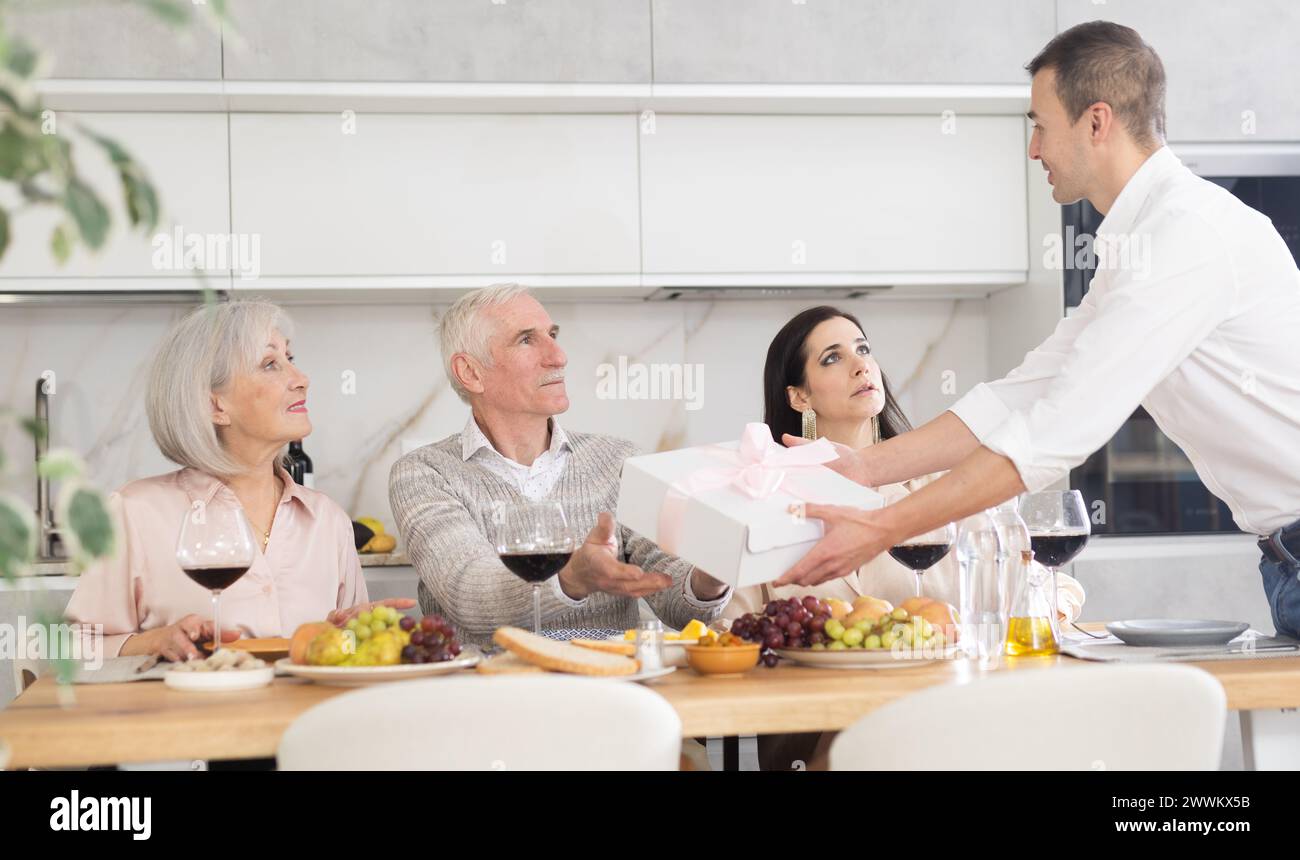 Young guy giving present to old man while sitting around kitchen table ...