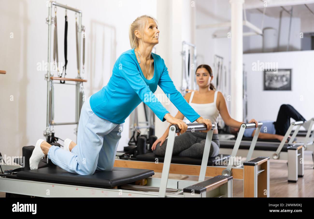 Focused aged woman lying with her legs and arms suspended while doing ...