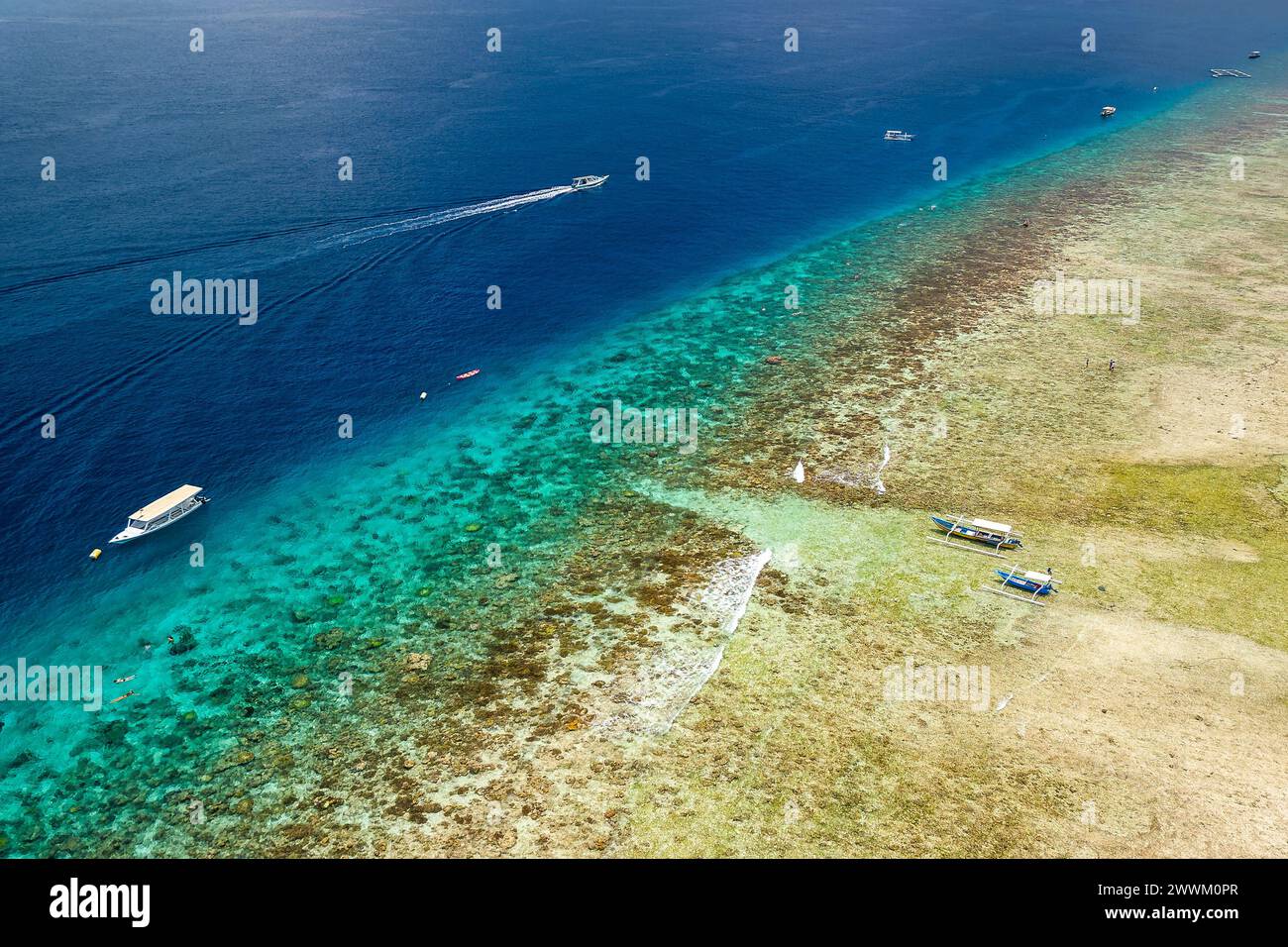 Tourist boats over a tropical coral reef at low tide on the coast of a ...