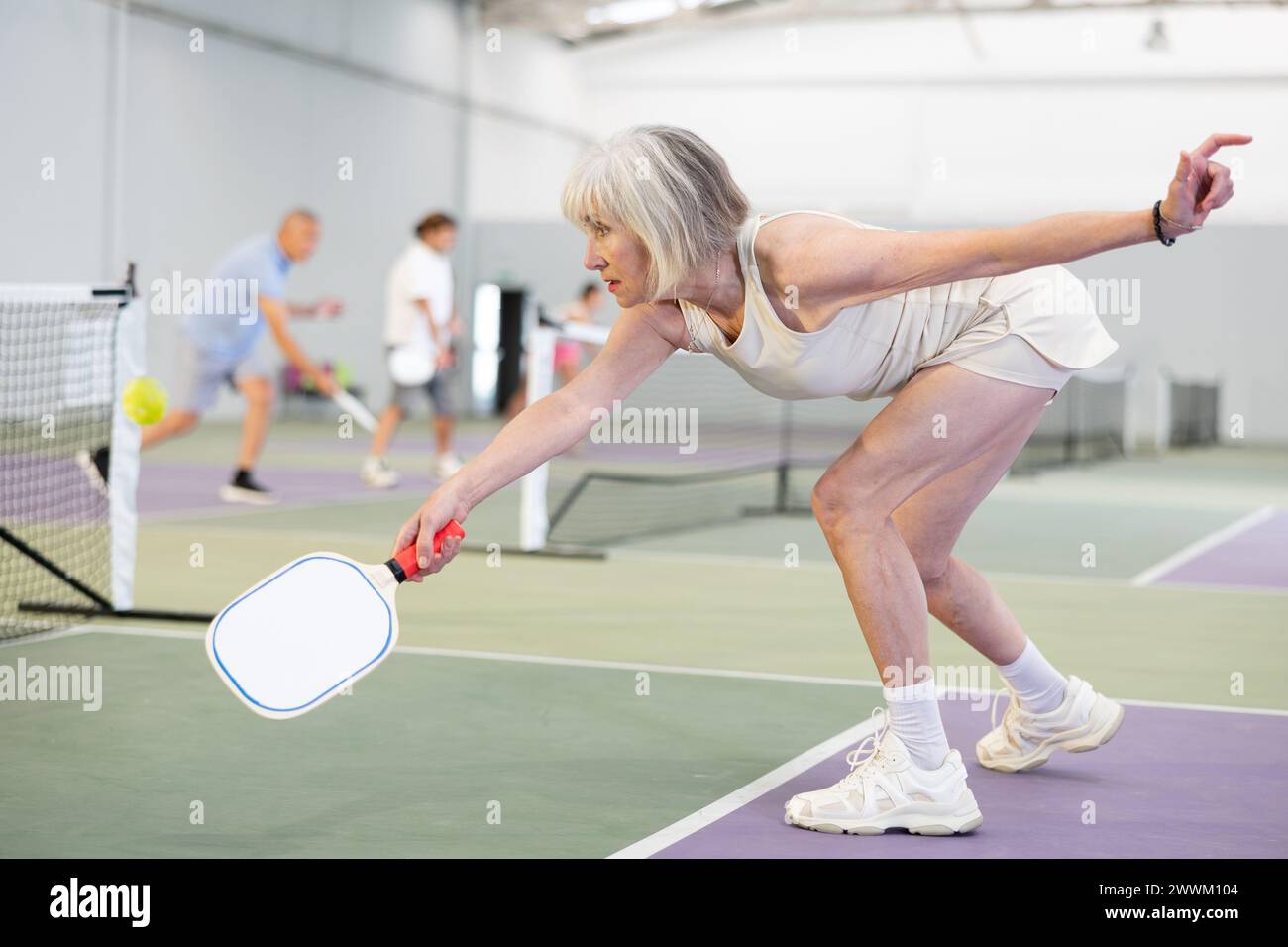 Positive elderly woman playing pickleball on indoor court Stock Photo ...