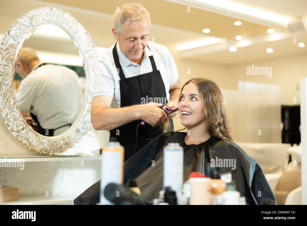 Experienced hairdresser using curling irons to create curls to young ...