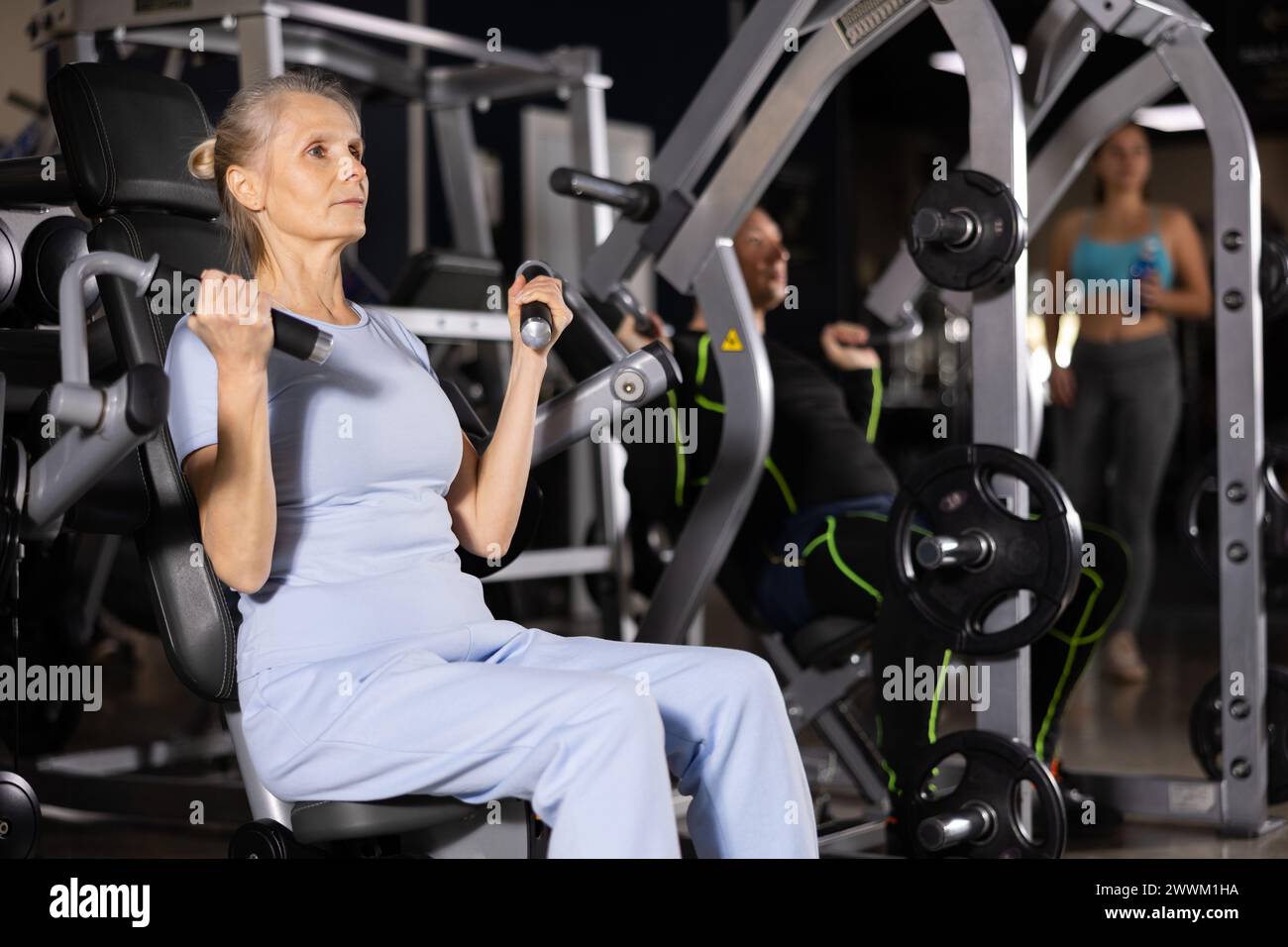 Sporty senior woman working out shoulders muscles on exercise machine ...