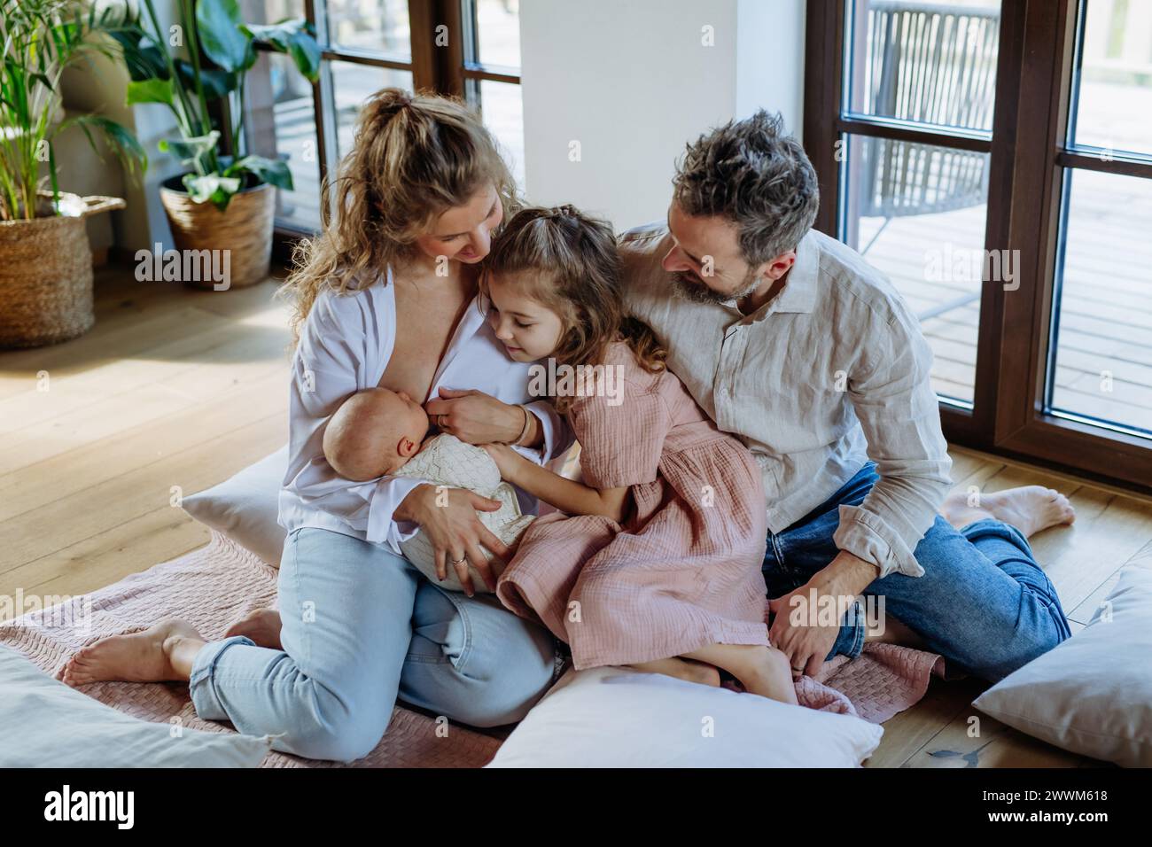 Mother breastfeeding newborn, big sister looking at new baby in mom's arms. Strong family ...