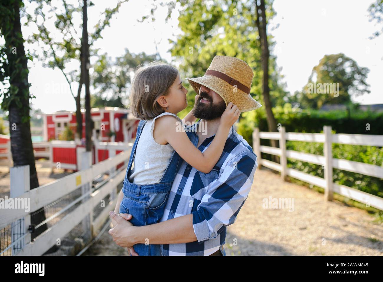 Farmer father and young daughter embracing, standing by wooden fence on ...