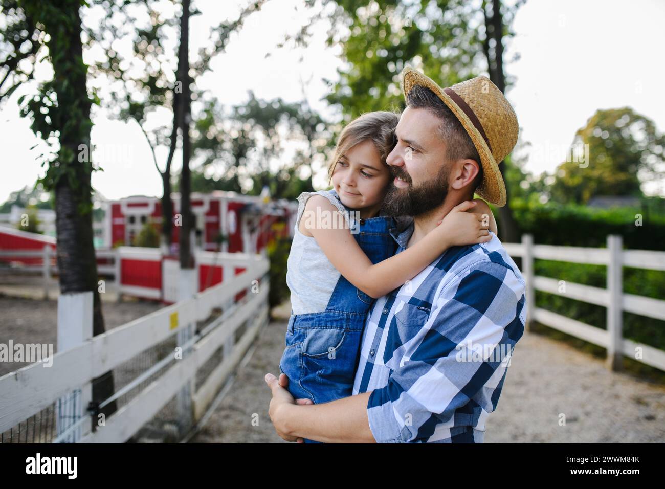 Farmer father and young daughter embracing, standing by wooden fence on ...