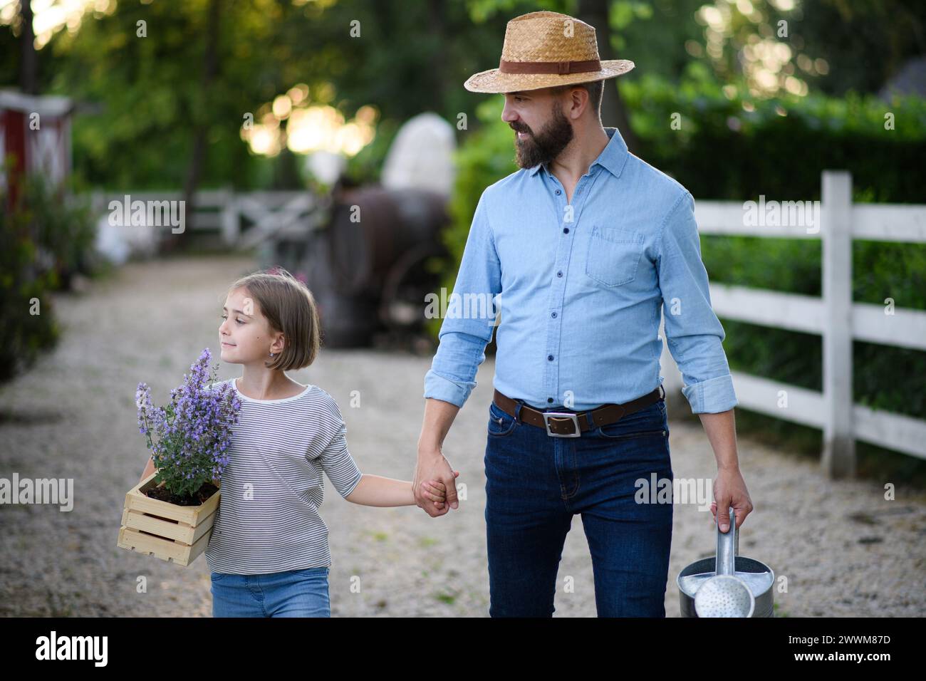 Father and young daughter walking across family farm, holding watering ...