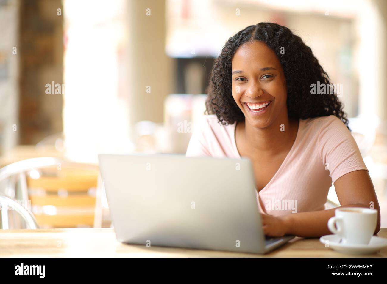 Happy black woman with laptop posing looking at you in a bar terrace ...