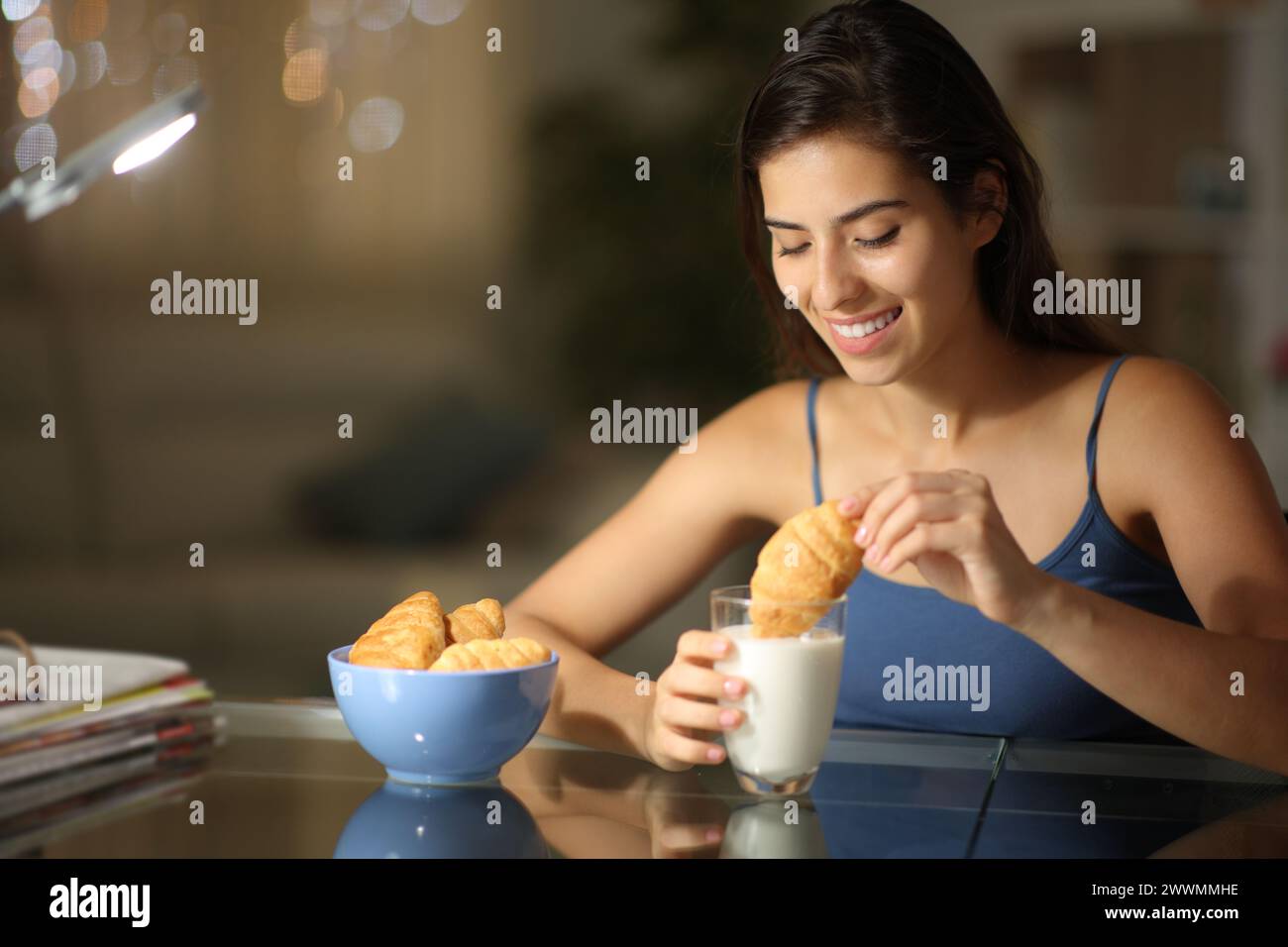 Happy woman in the night dipping bakery in milk at home Stock Photo - Alamy