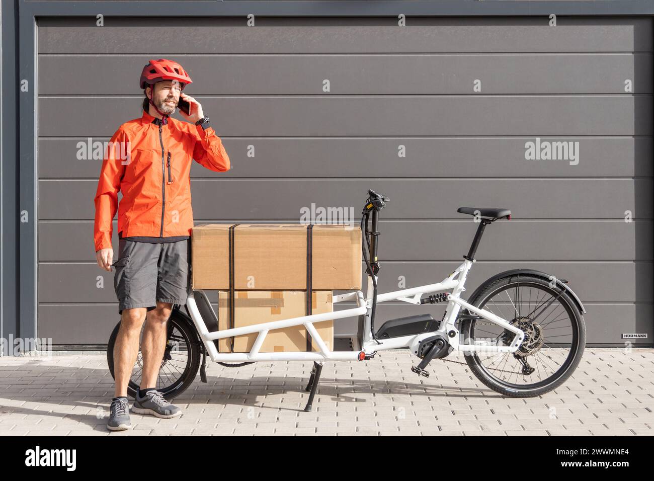 young courier with red clothing and helmet riding cargo bike arriving ...