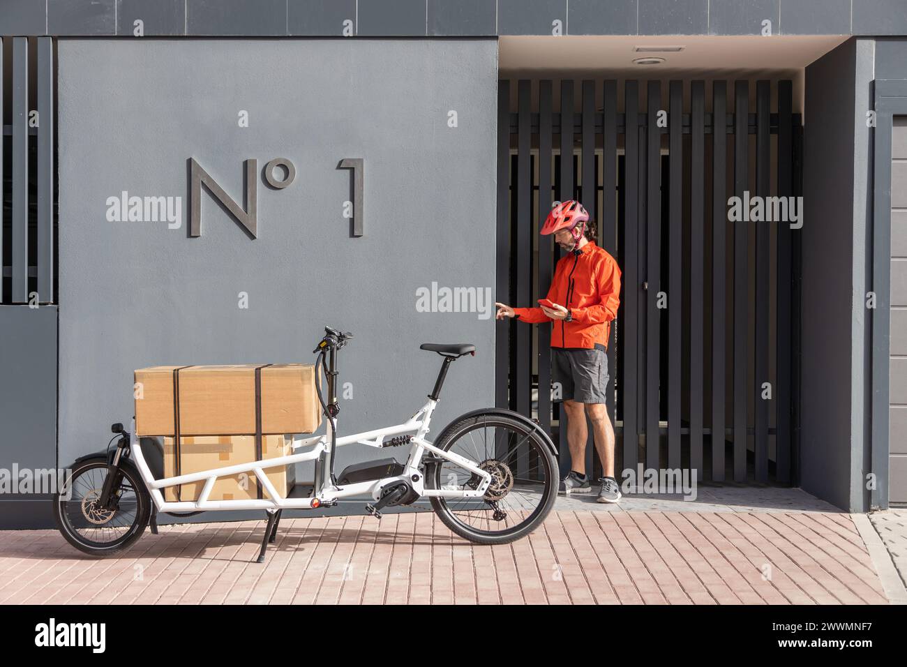 young courier with red clothing and helmet riding cargo bike arriving ...