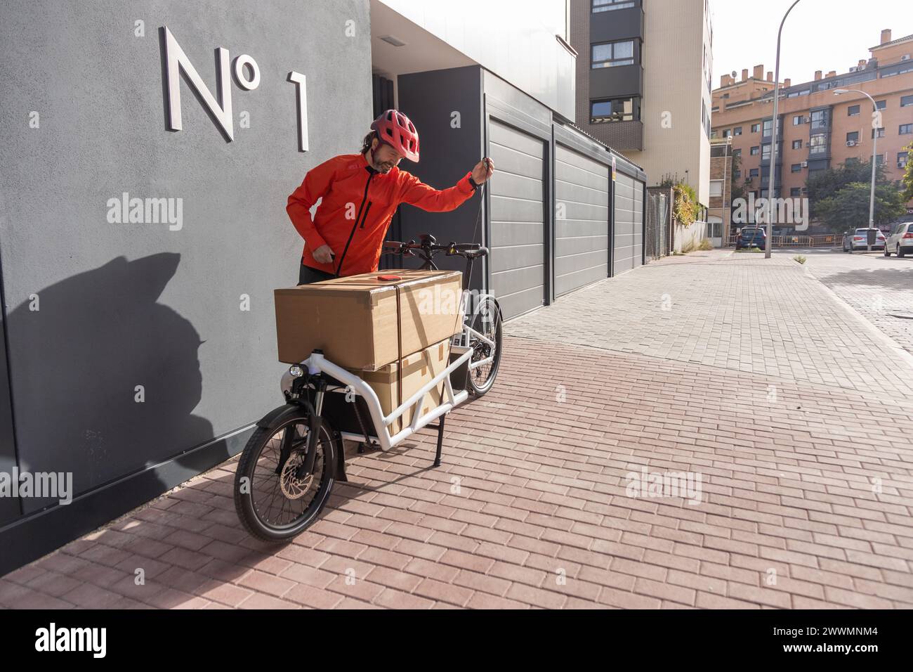 young courier with red clothing and helmet riding cargo bike arriving ...