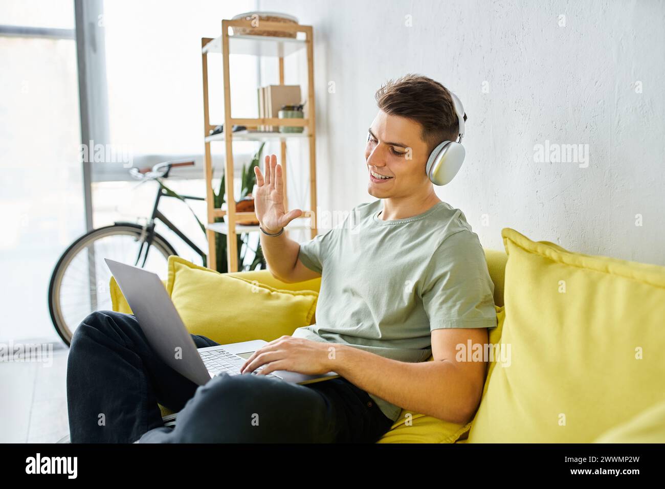 smiling young guy with headphones and laptop in yellow couch saying ...