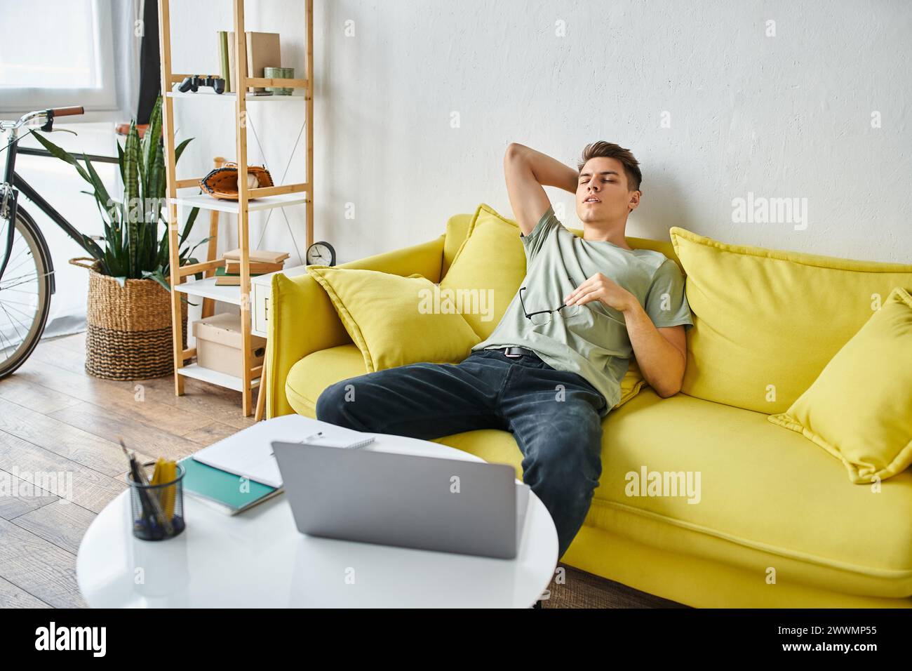 weary guy with laptop putting hand behind head and leaning on yellow ...