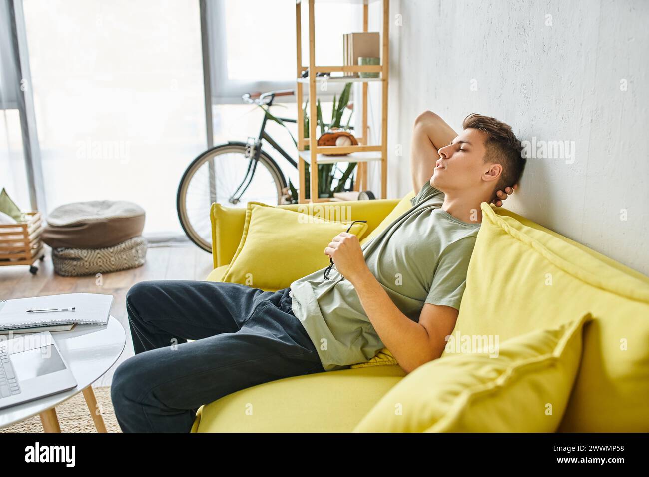 sideways of weary man in his 20s putting hand behind head and leaning ...